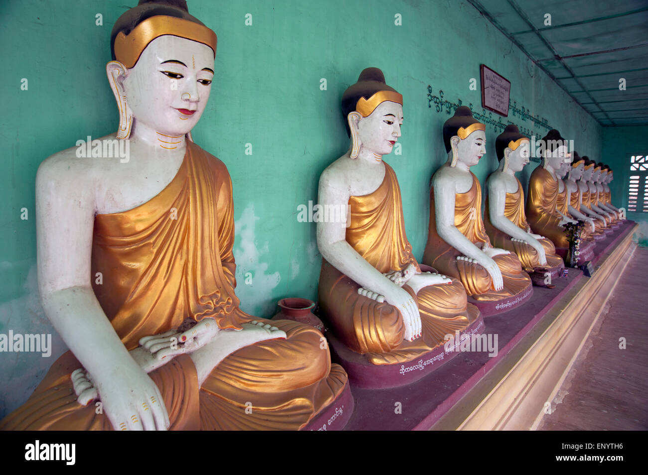 Long row of painted stone Buddhas against a green temple wall in the ...