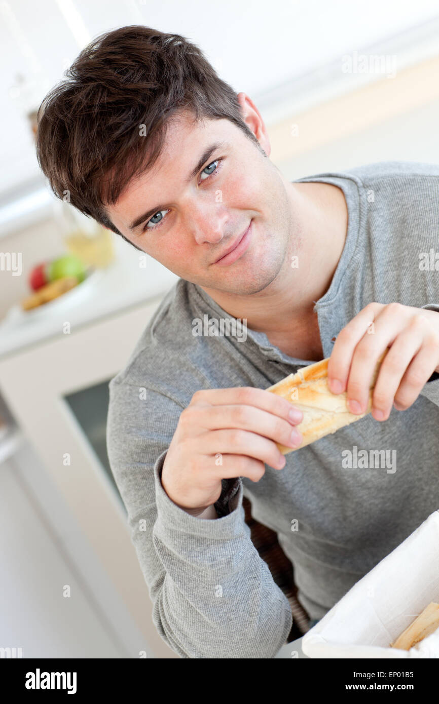 attractive young man eating bread sitting in his kitchen Stock Photo ...
