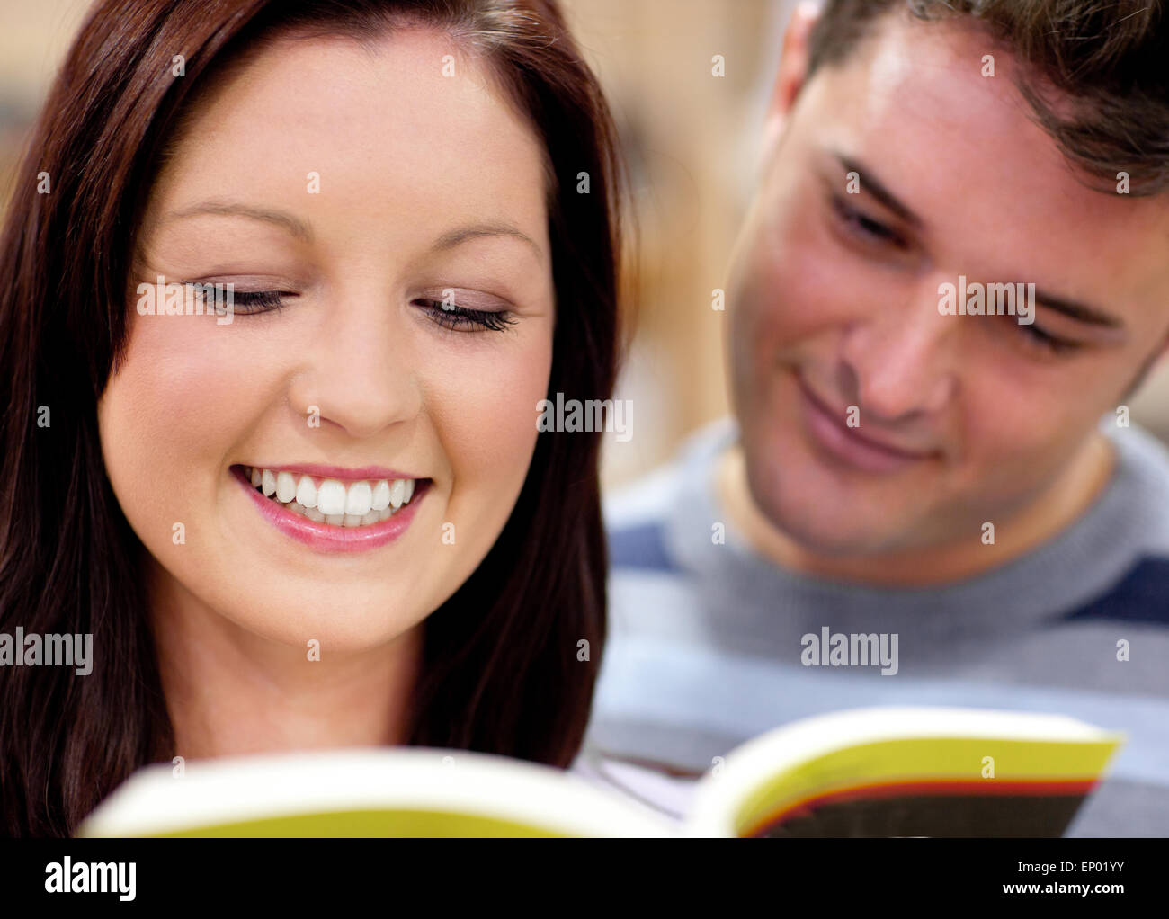 Close-up of a smiling couple of students reading a book in a bookstore ...