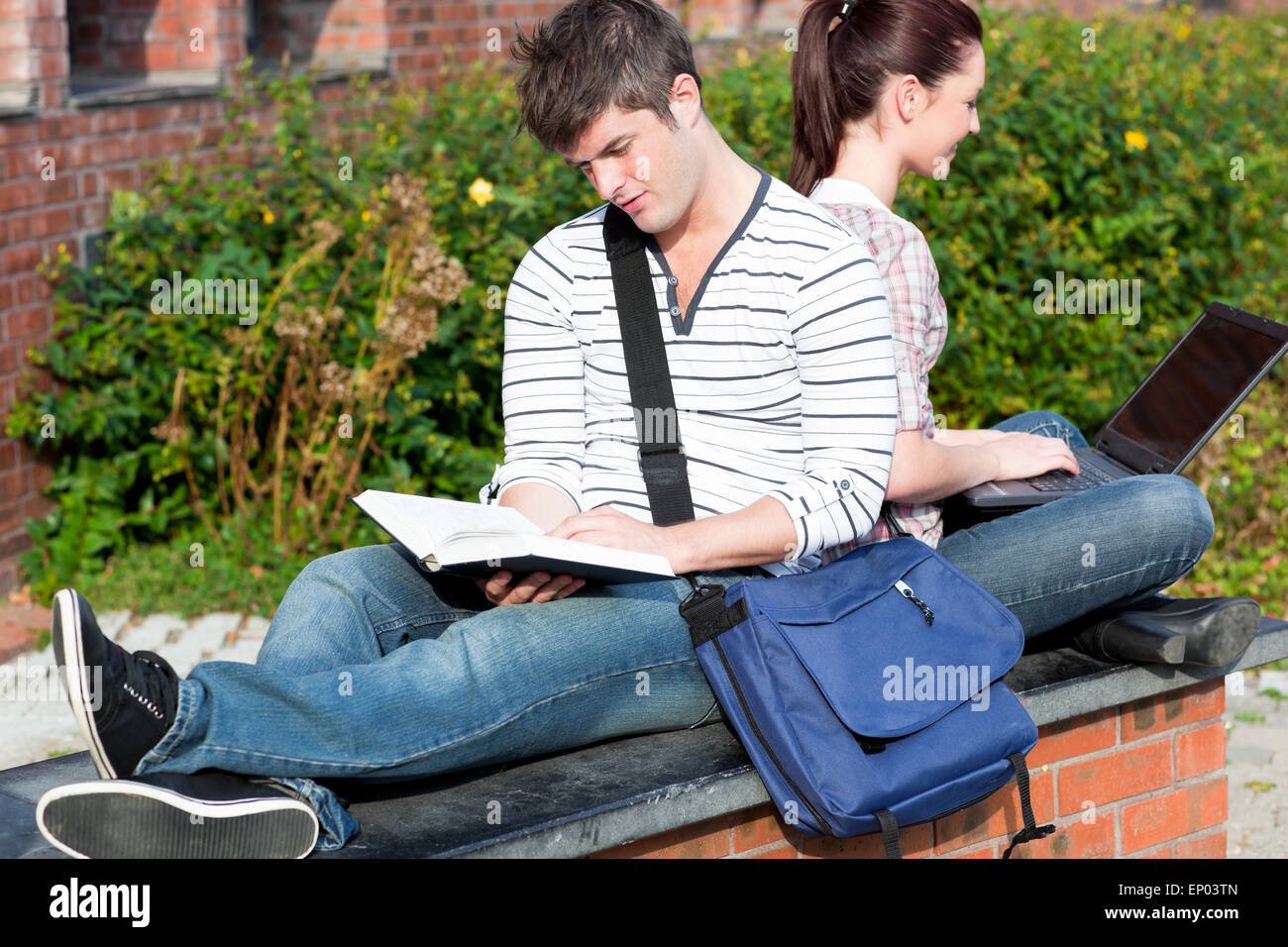 Couple of students using a laptop and reading a book sitting Stock ...