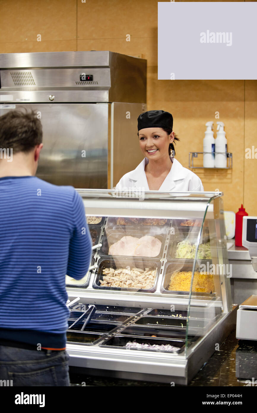 Female cook waiting for a student to choose his lunch in the cafeteria ...
