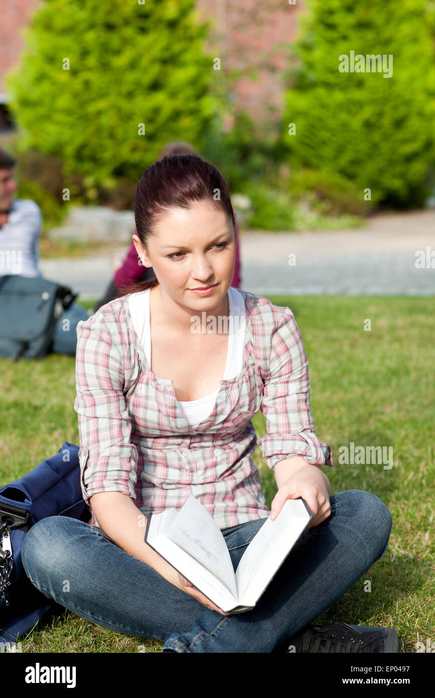 Thoughtful female student reading a book sitting on grass Stock Photo ...