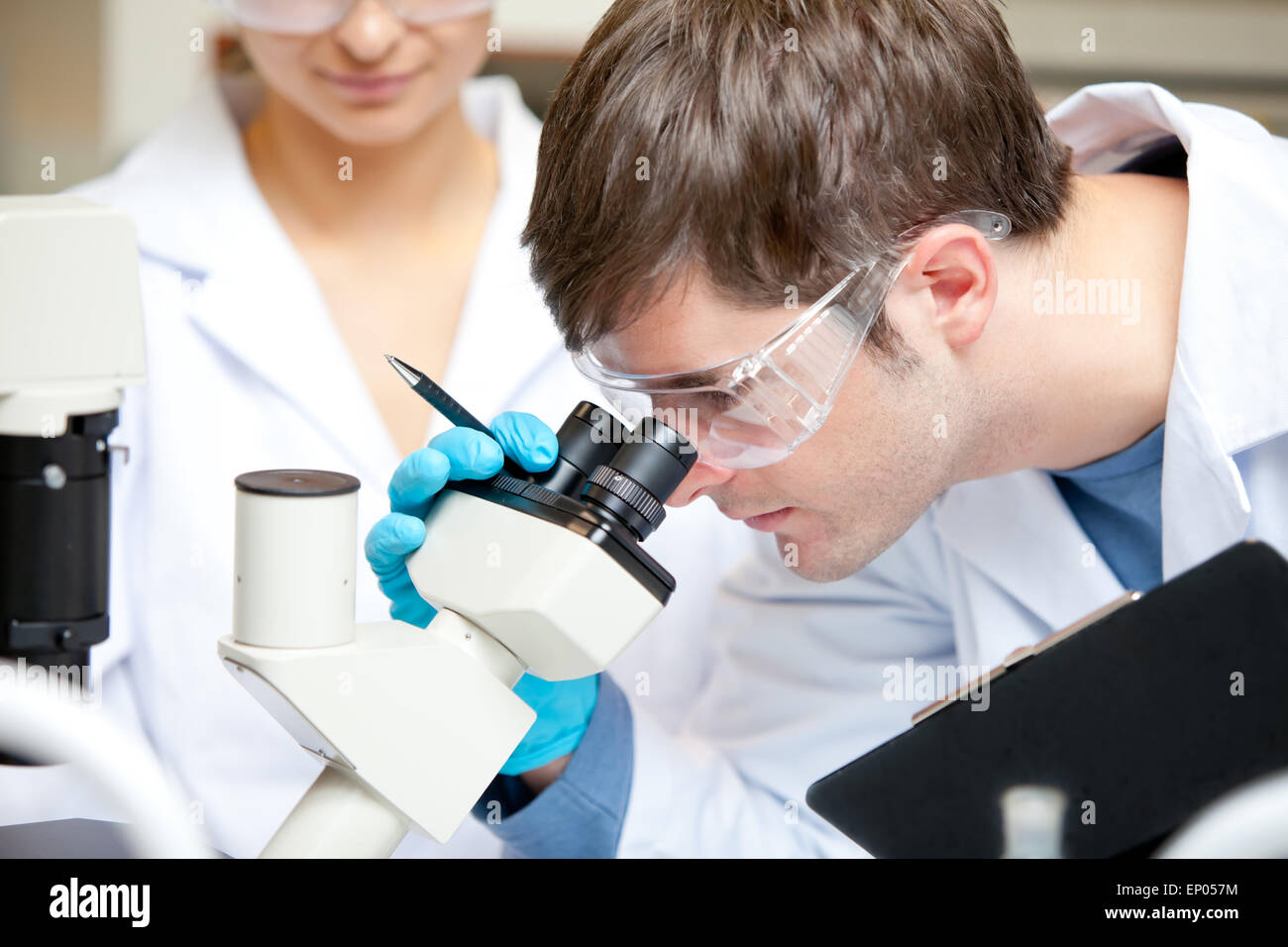 Caucasian male scientist holding pen and clipboard looking through a ...