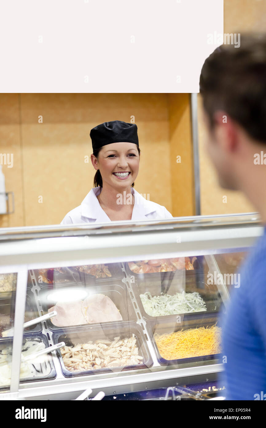 Joyful baker behind her display and customer in the queue talking ...