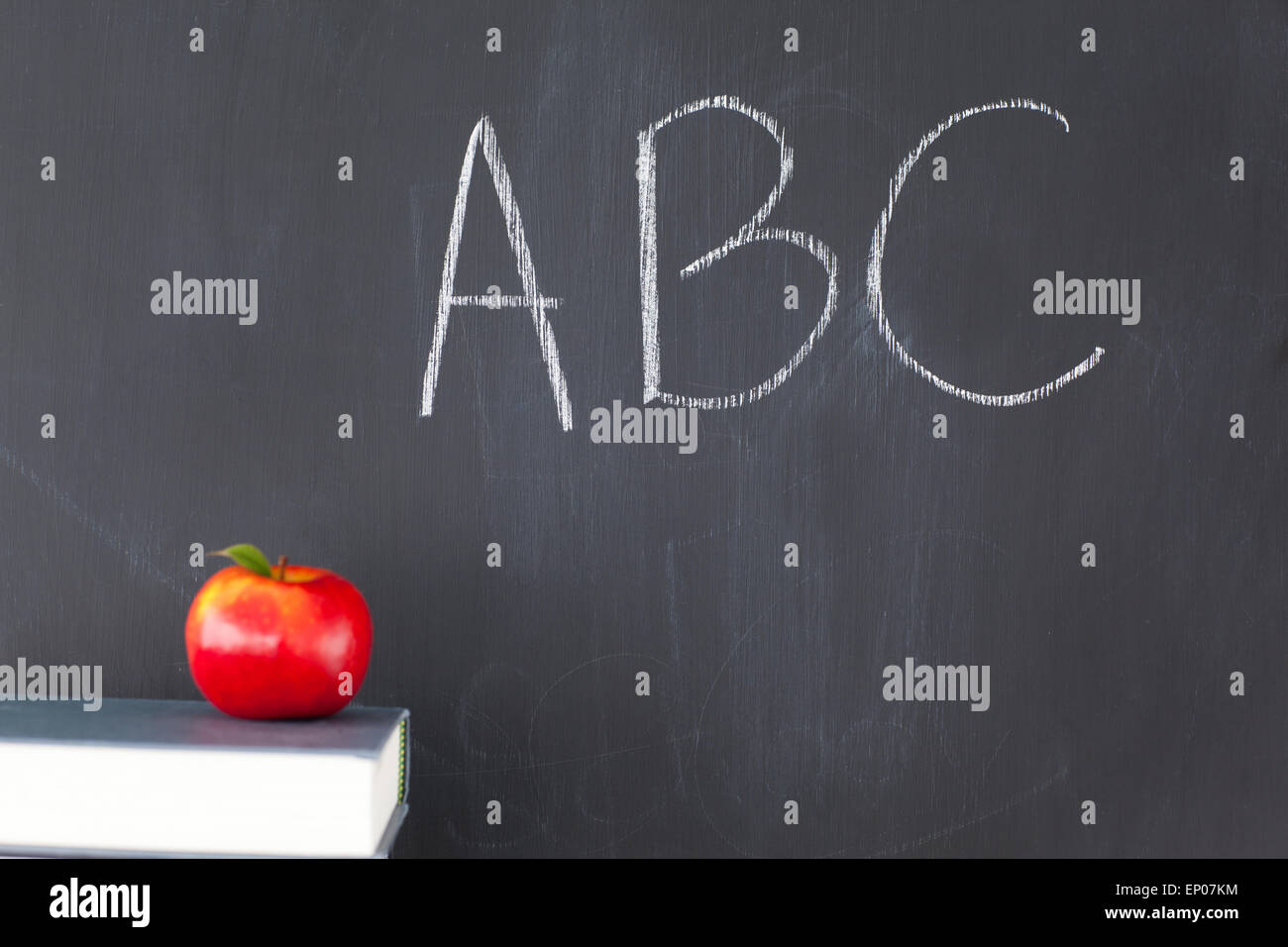 Stack of books with a red apple and a blackboard with ABC written on it ...
