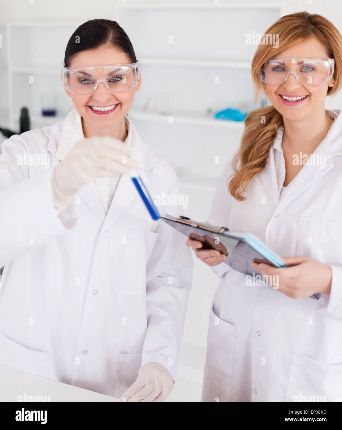 Two scientists looking at the camera while holding a test tube and a ...