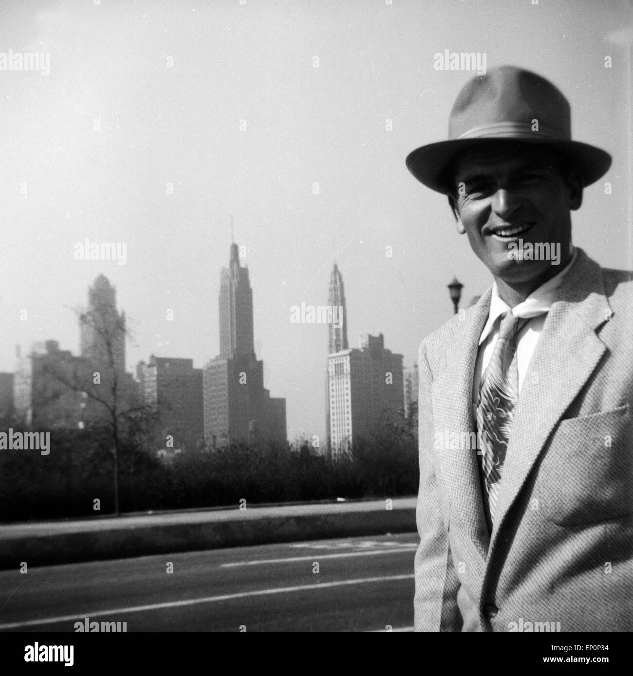 Ein Mann steht lachend vor der Skyline einer Stadt in den USA, 1954. A ...