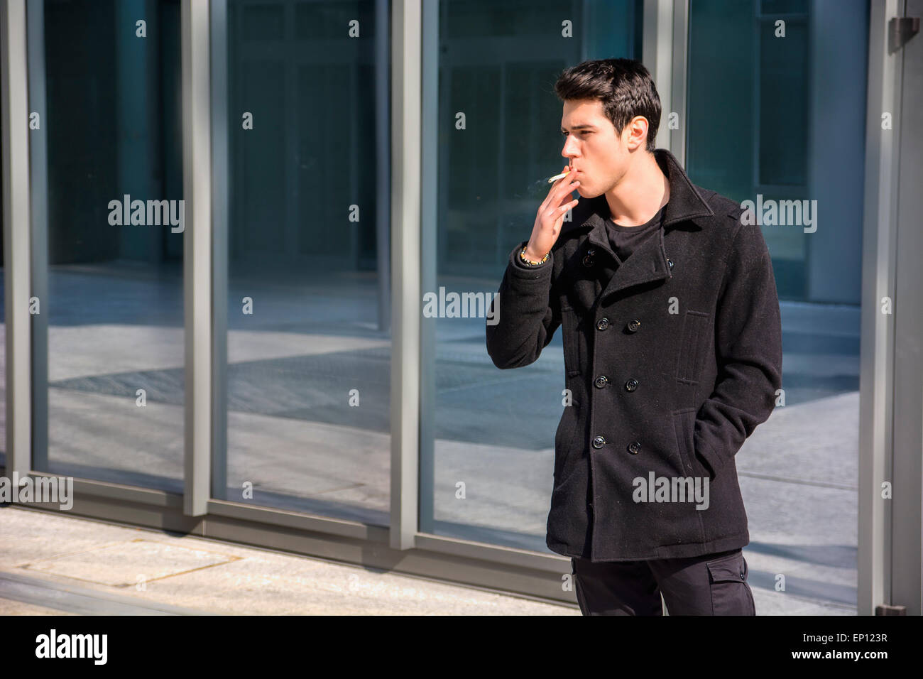 Handsome stylish young man smoking outside in urban setting, looking ...