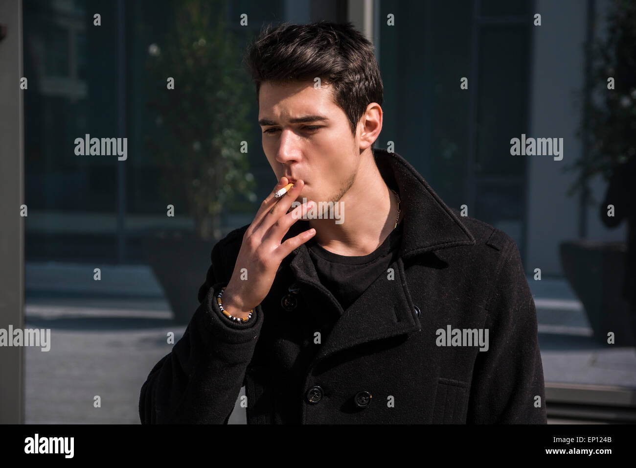 Handsome stylish young man smoking outside in urban setting, looking ...