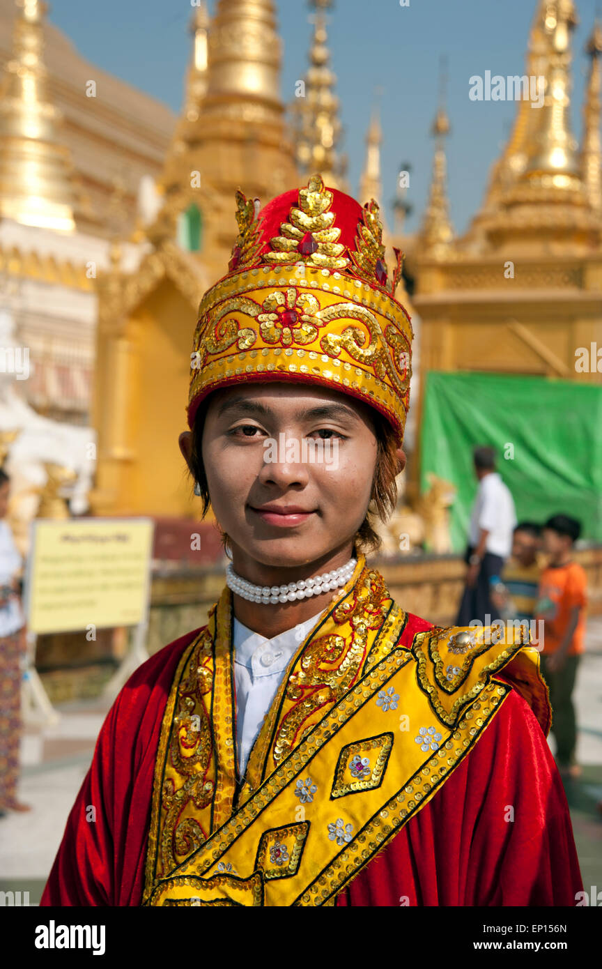 Portrait of a Burmese man in traditional costume in front of gold spires at the Shwedagon Pagoda ...