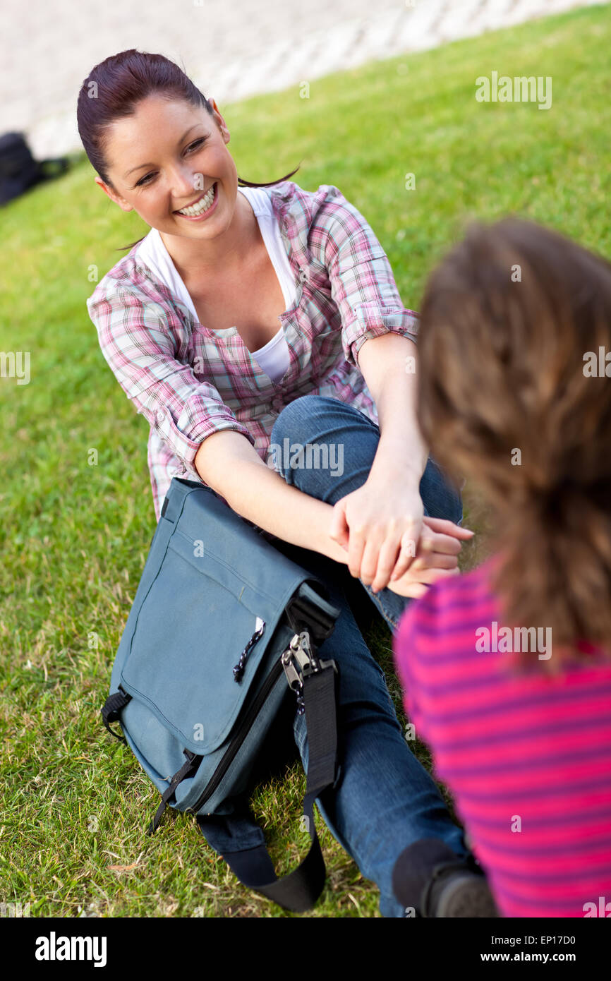 Two female students talking together sitting on the grass Stock Photo ...