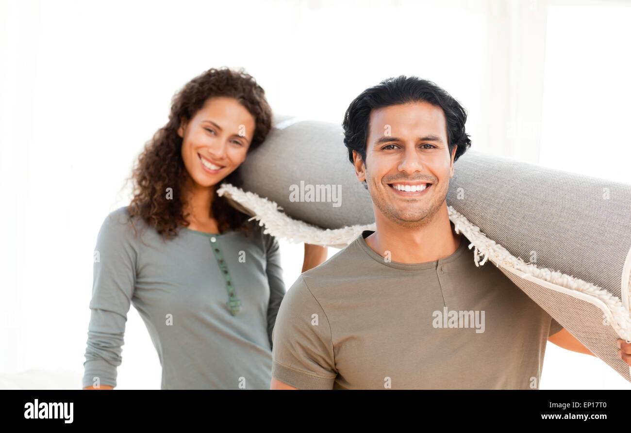 Cute couple carrying a carpet standing in the living room Stock Photo ...
