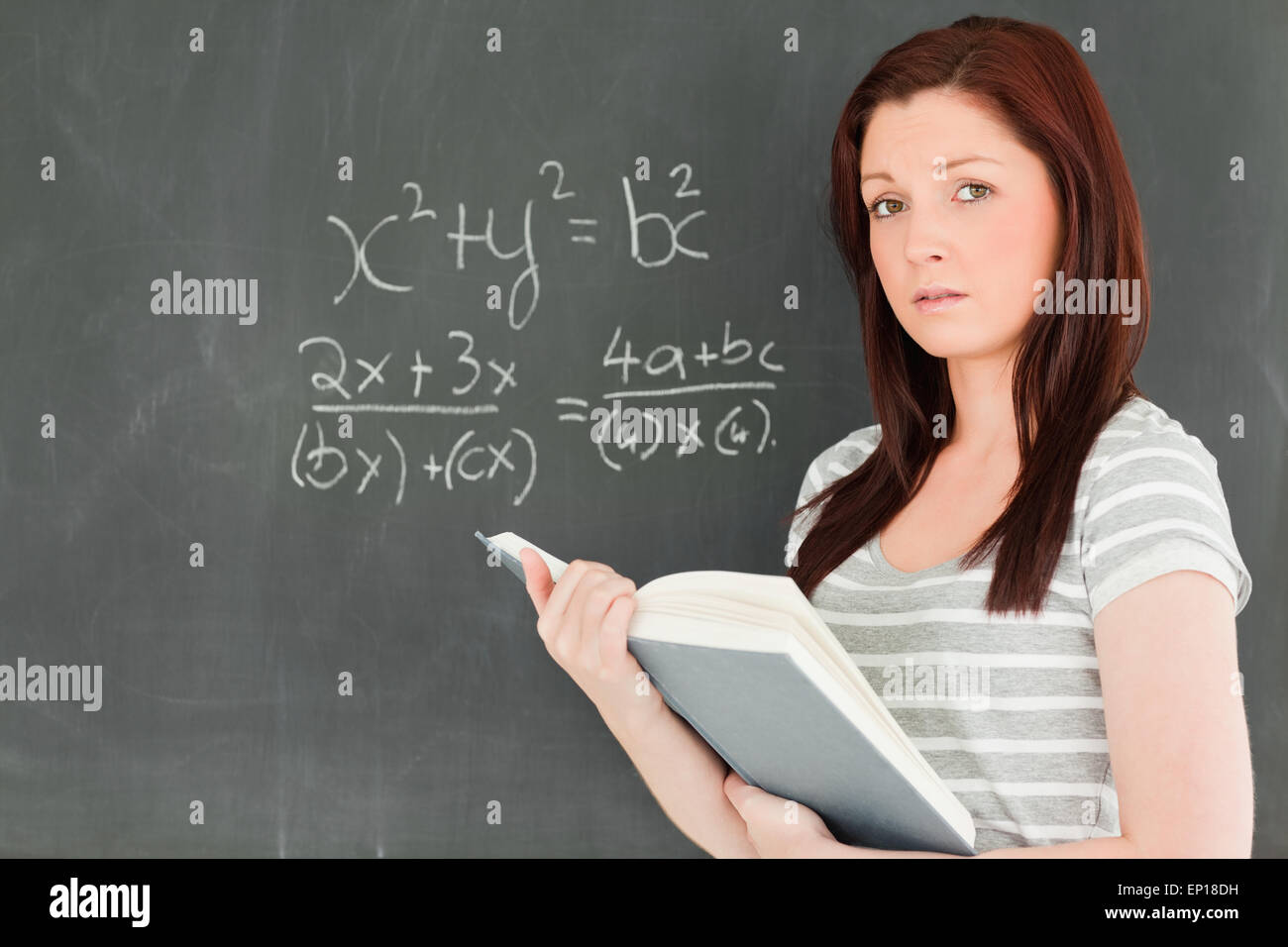 Cute woman trying to solve a mathematical equation on a blackboard ...