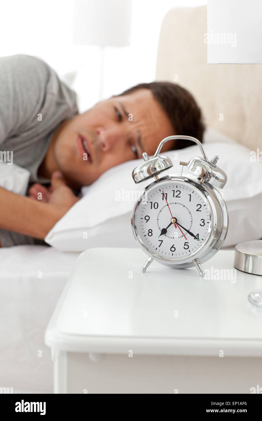 Unhappy man looking at his alarm clock while lying on his bed Stock ...