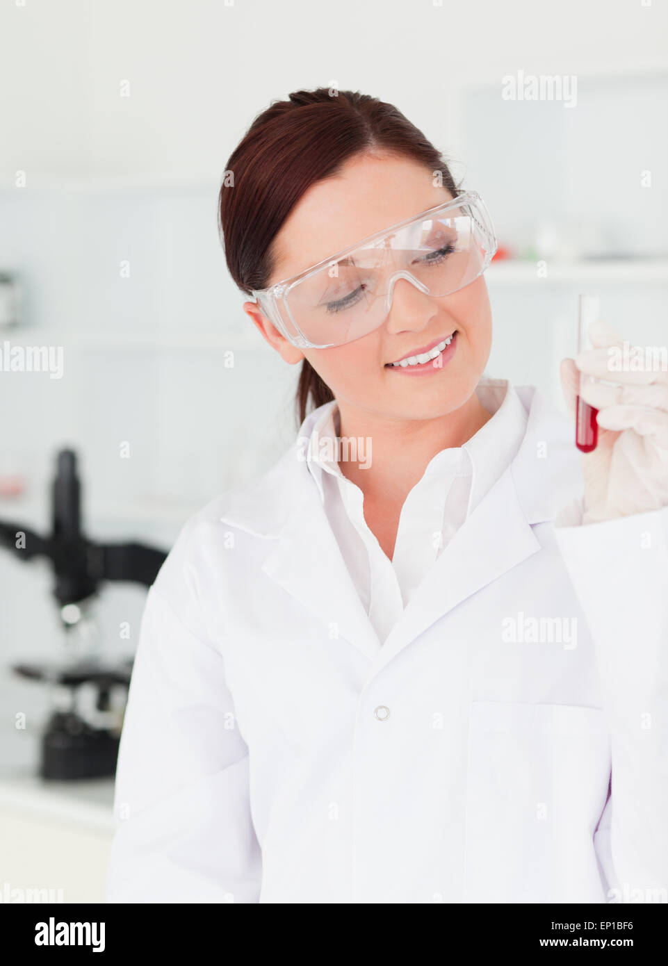 Pretty red-haired scientist looking at the camera while holding a test ...