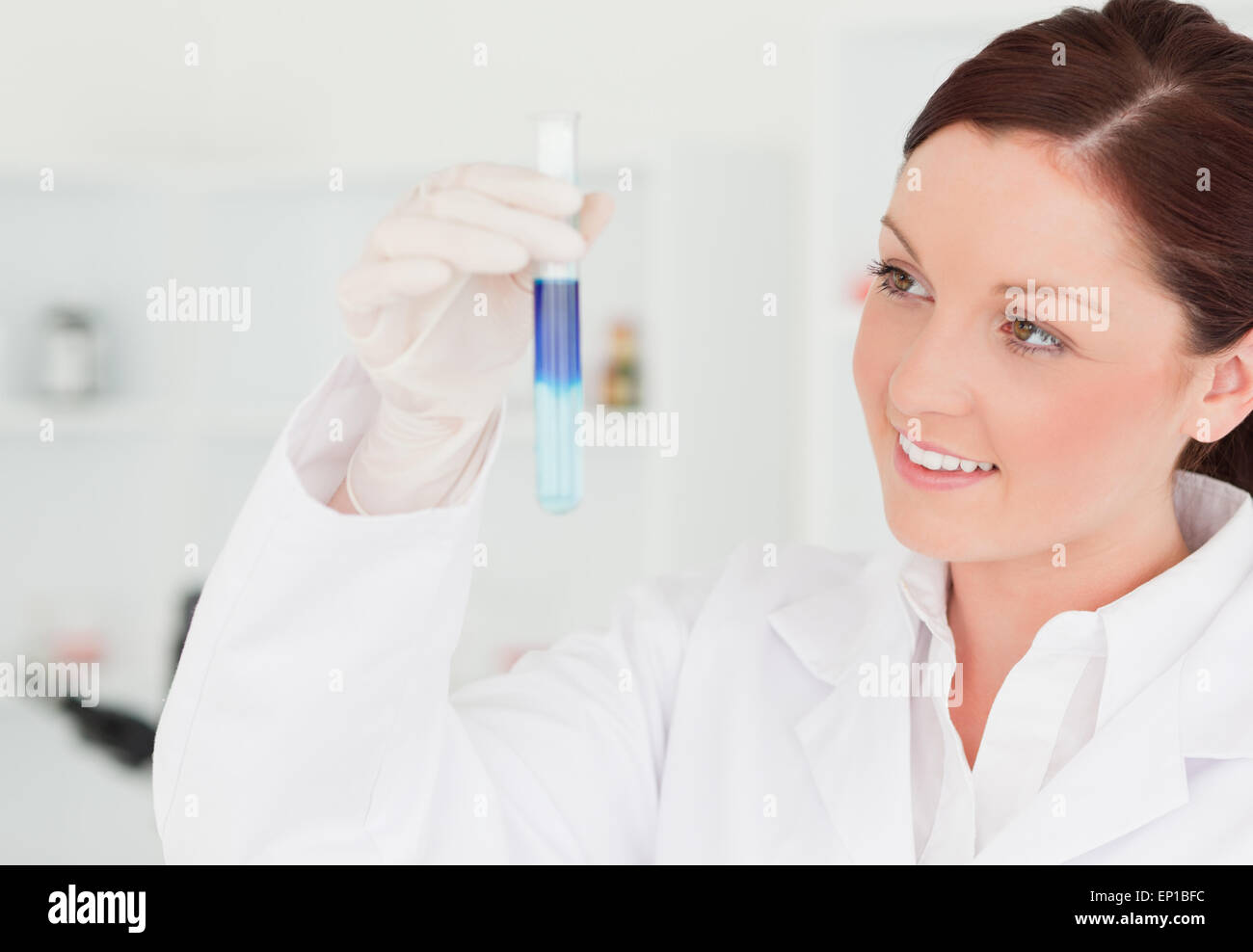 Smiling red-haired scientist looking at the camera while holding a test ...