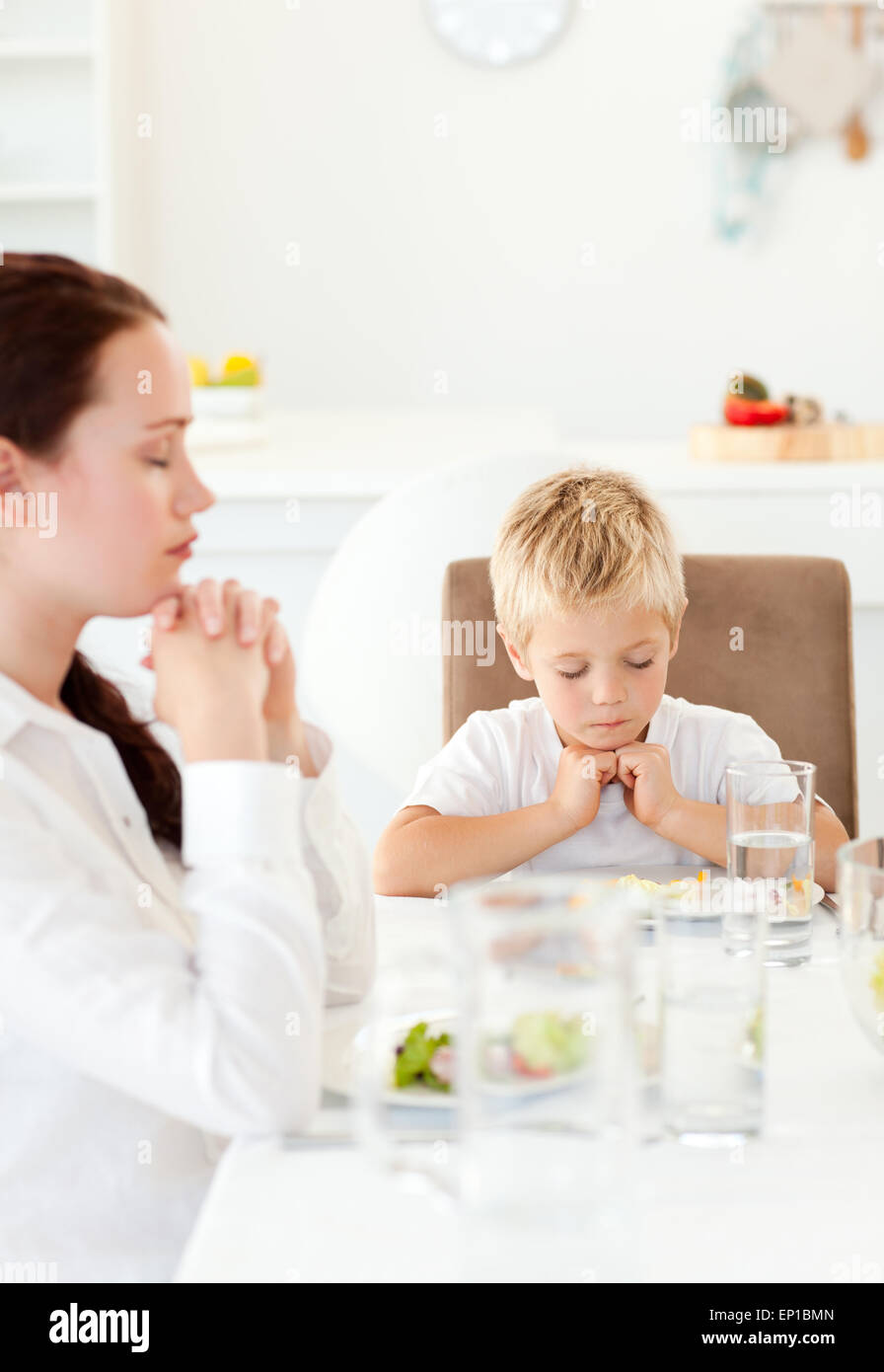 Concentrated little boy praying with his mother before eating their ...