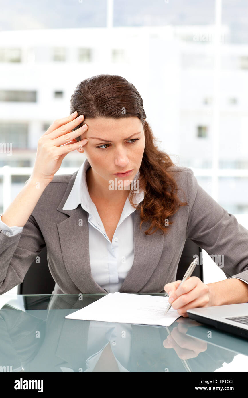 Concentrated businesswoman taking notes while working on her laptop ...