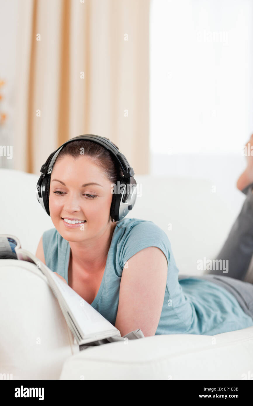 Attractive woman with headphones reading a magazine while lying on a ...