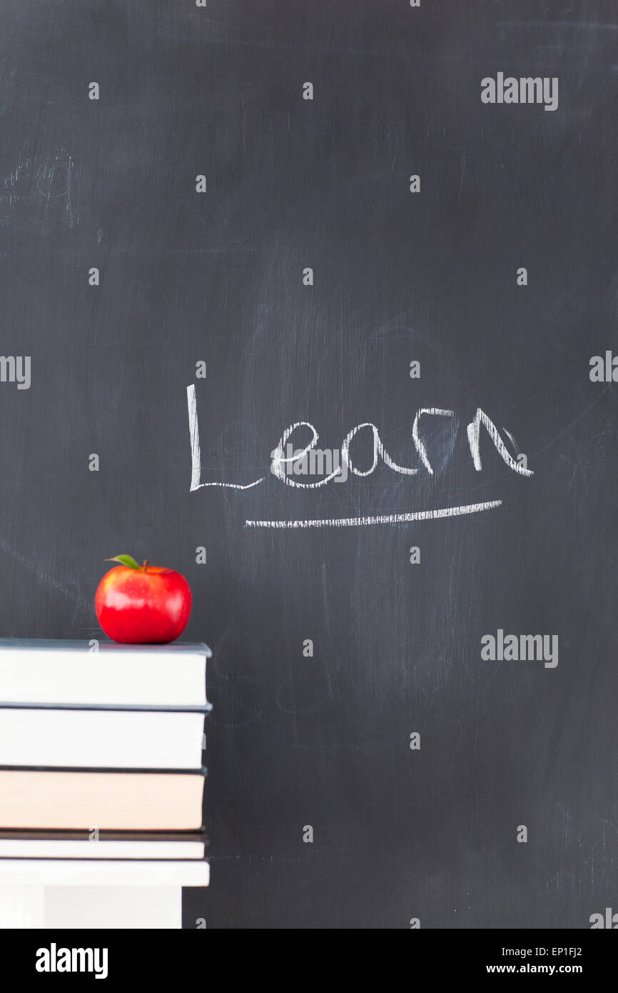 Stack of books with a red apple and a blackboard with learn written on ...