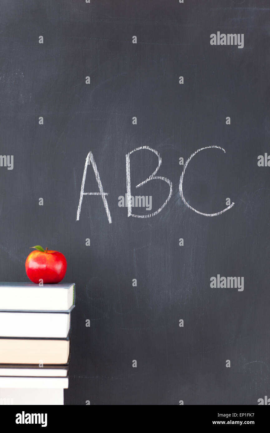 Stack of books with a red apple and a blackboard with ABC written on it ...
