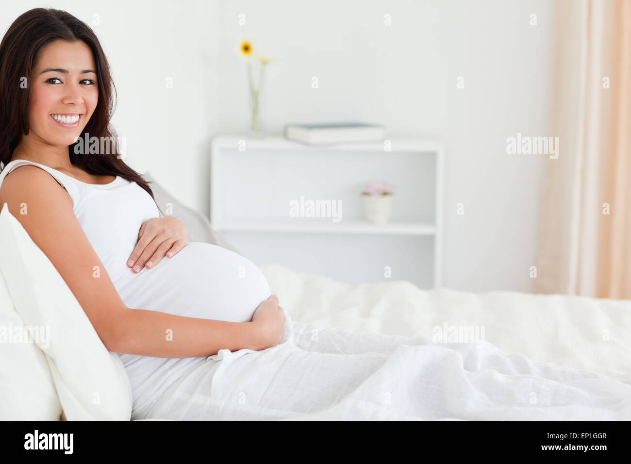 Good looking pregnant woman touching her belly while lying on a bed ...