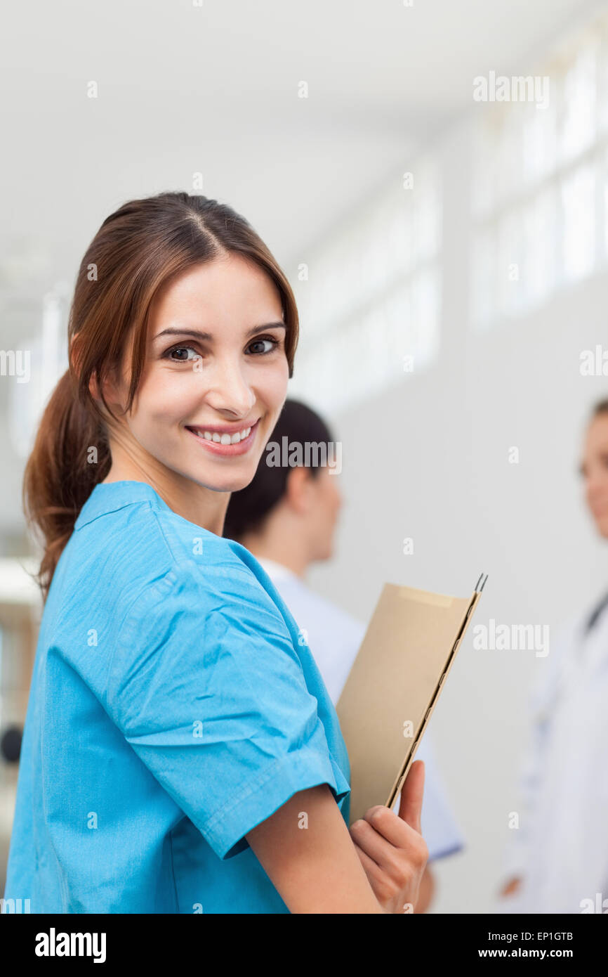 Nurse smiling while holding files and standing with a doctor and a ...