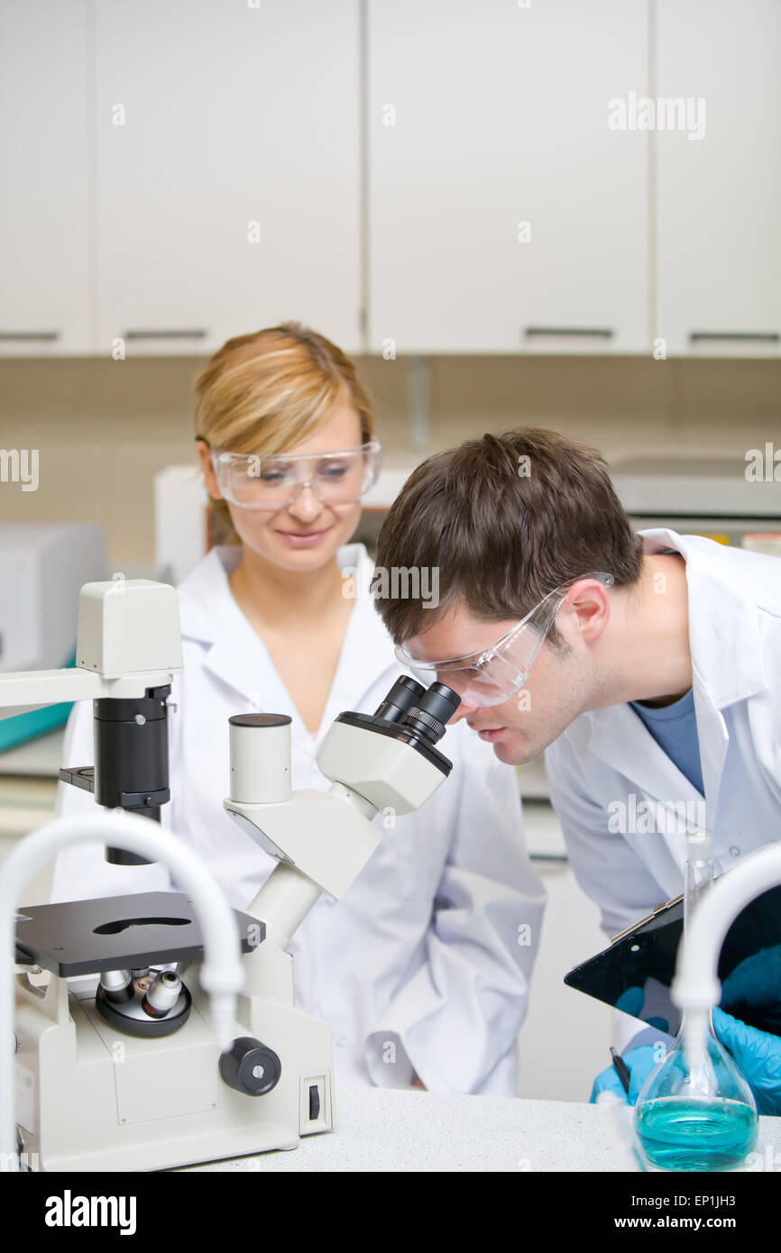 Caucasian scientists holding clipboard and looking through a microscope ...