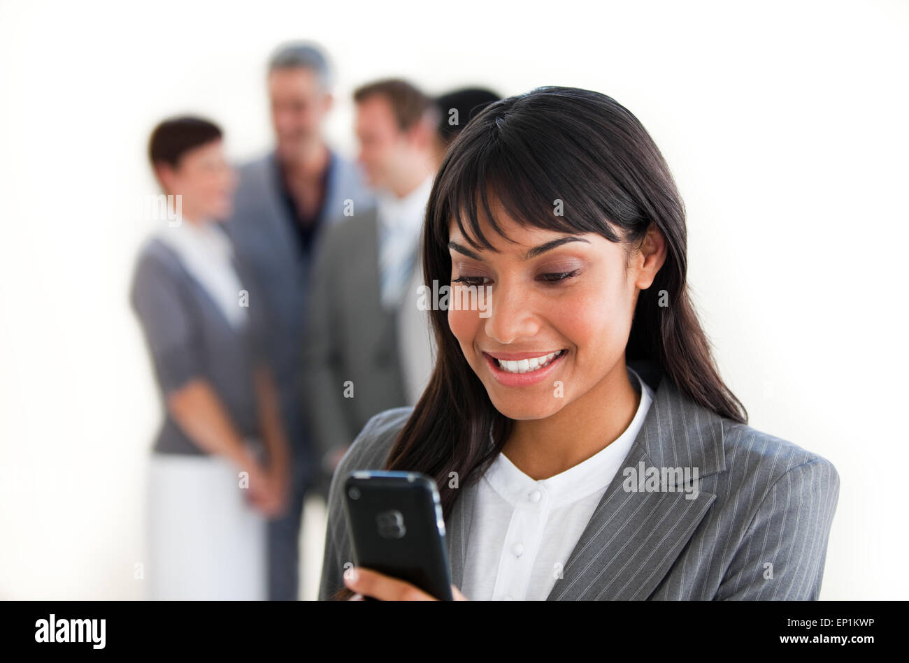 Smiling businesswoman sending a text in front of her team Stock Photo ...