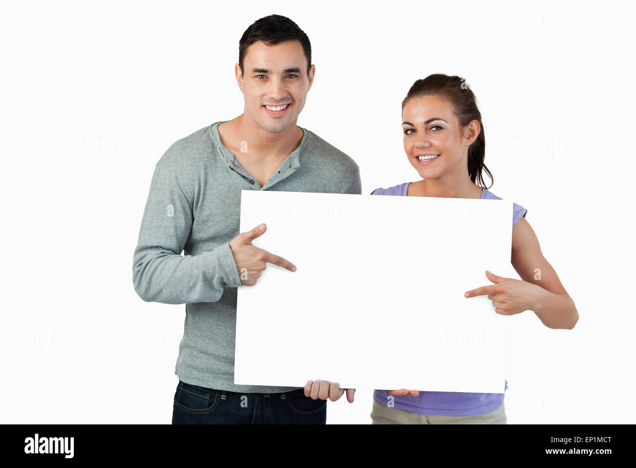 Smiling young couple pointing at sign they are holding Stock Photo - Alamy