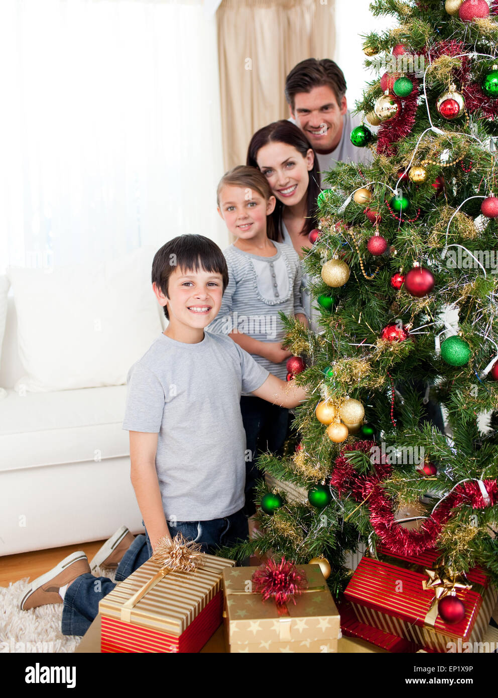 Happy family decorating a Christmas tree with boubles and presents ...