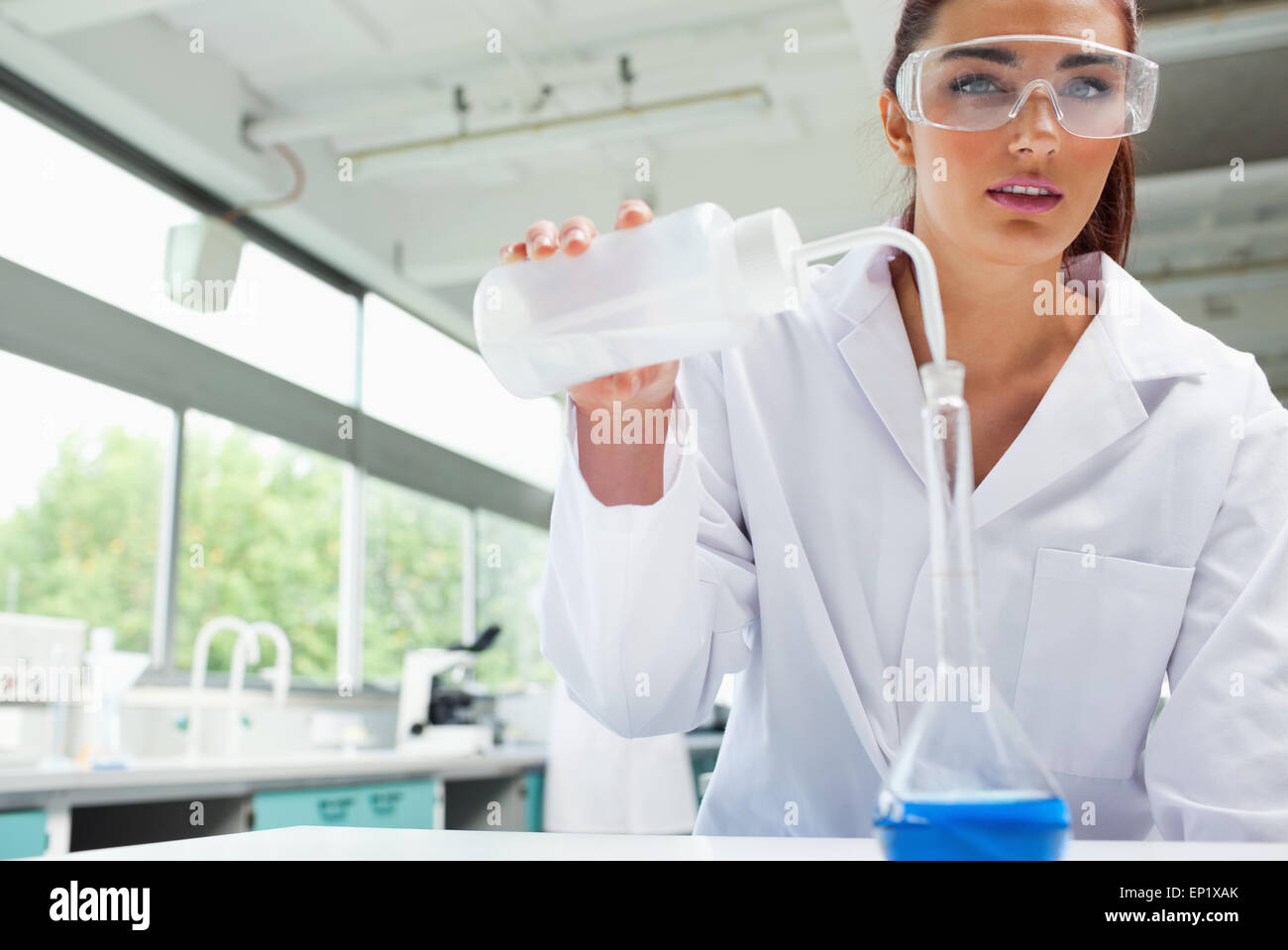 Female science student pouring liquid with protective glasses Stock ...