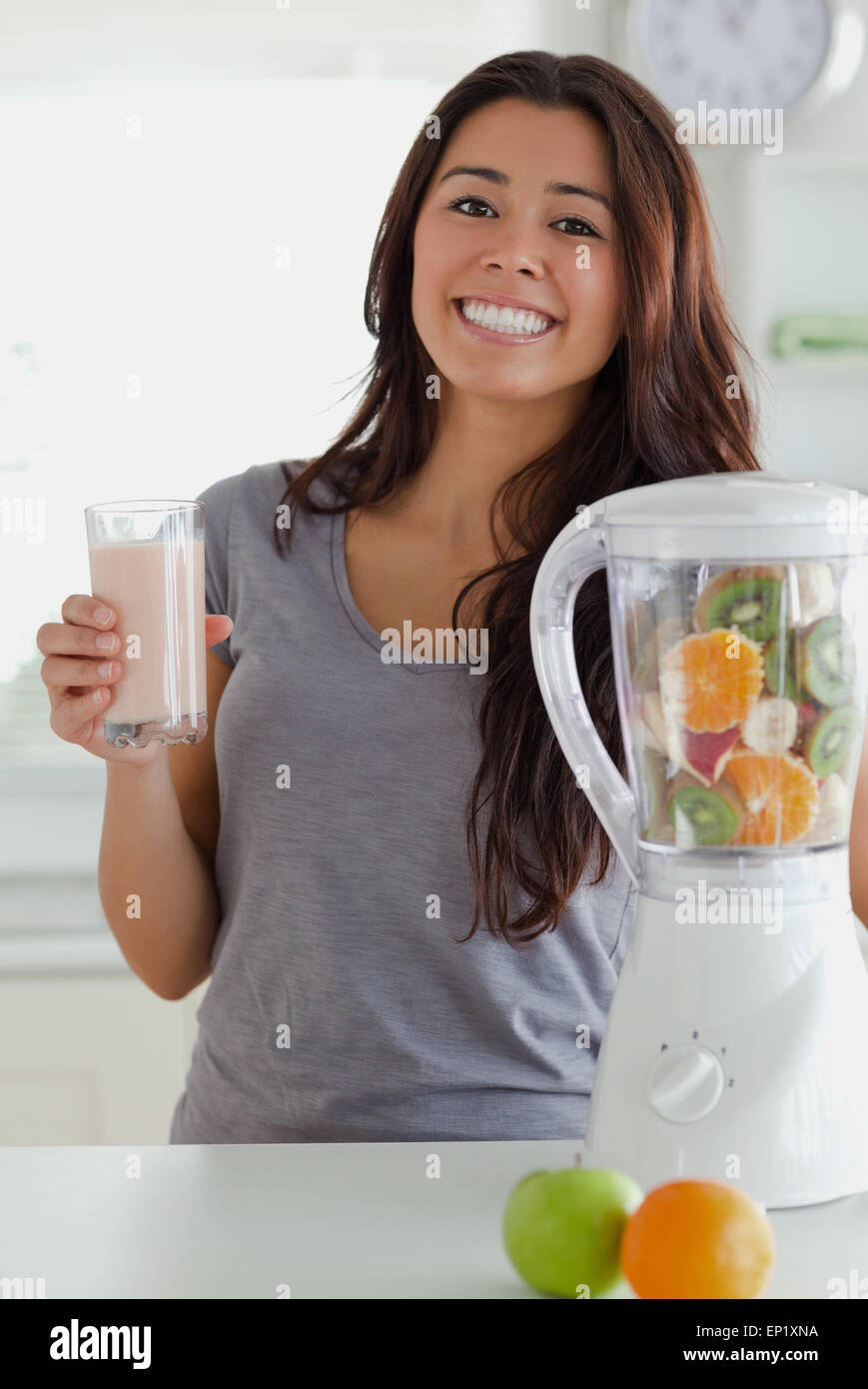 Lovely woman using a blender while holding a drink Stock Photo - Alamy