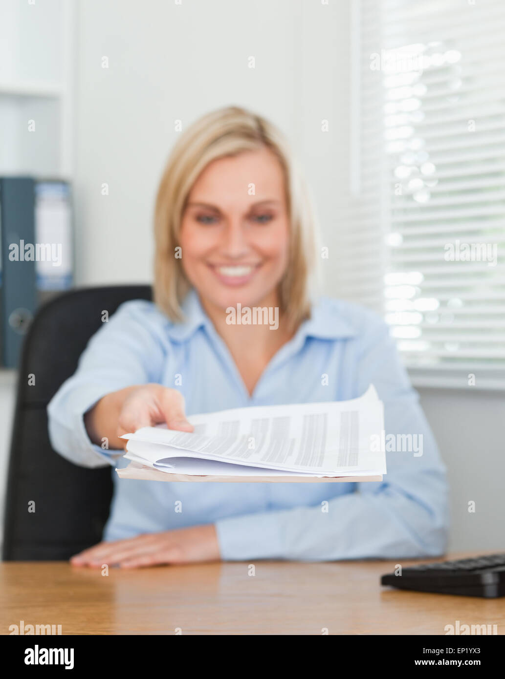 Smiling blonde businesswoman passing a paper looking at it Stock Photo ...