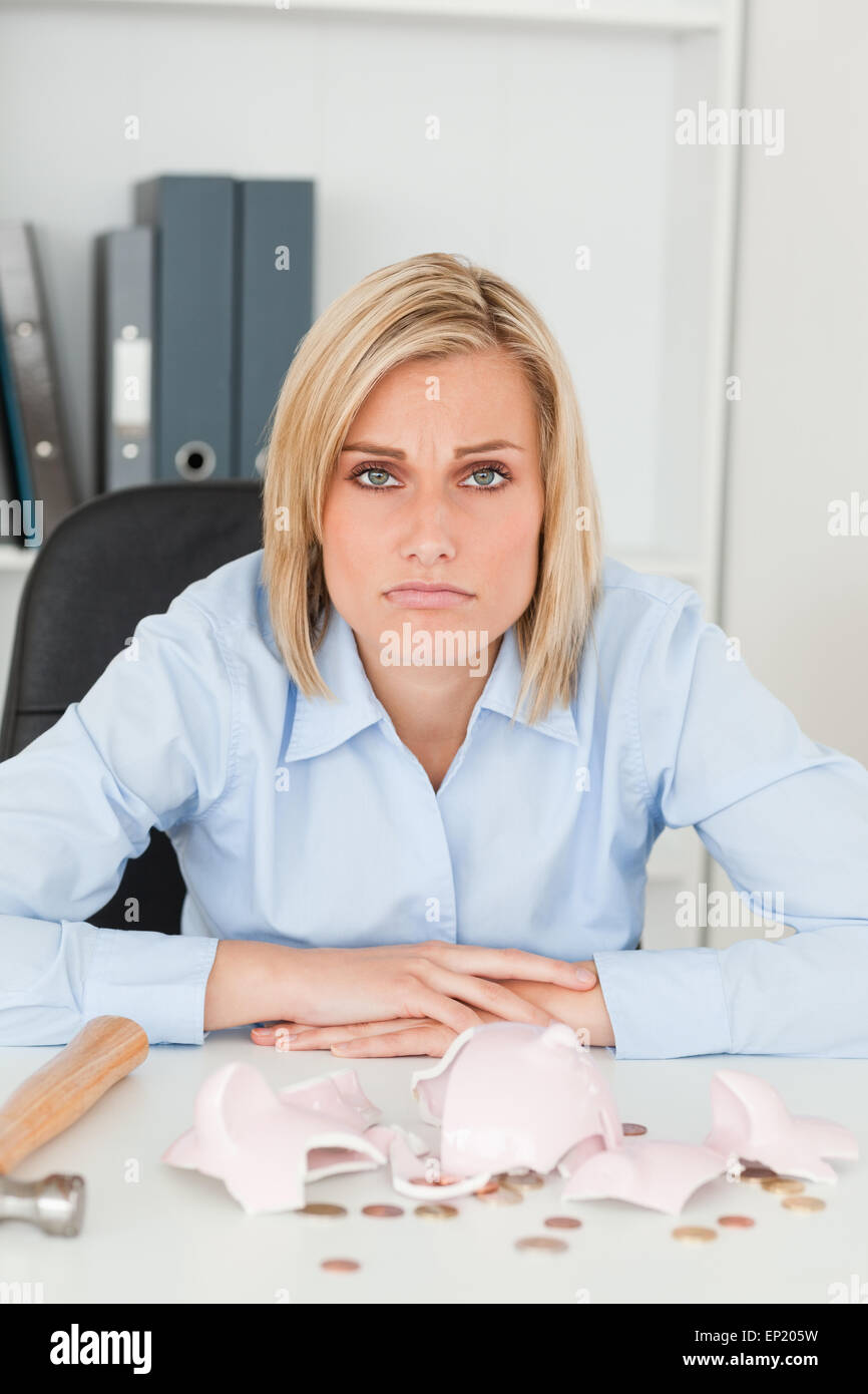 Sulking woman sitting in front of an shattered piggy bank looking into ...