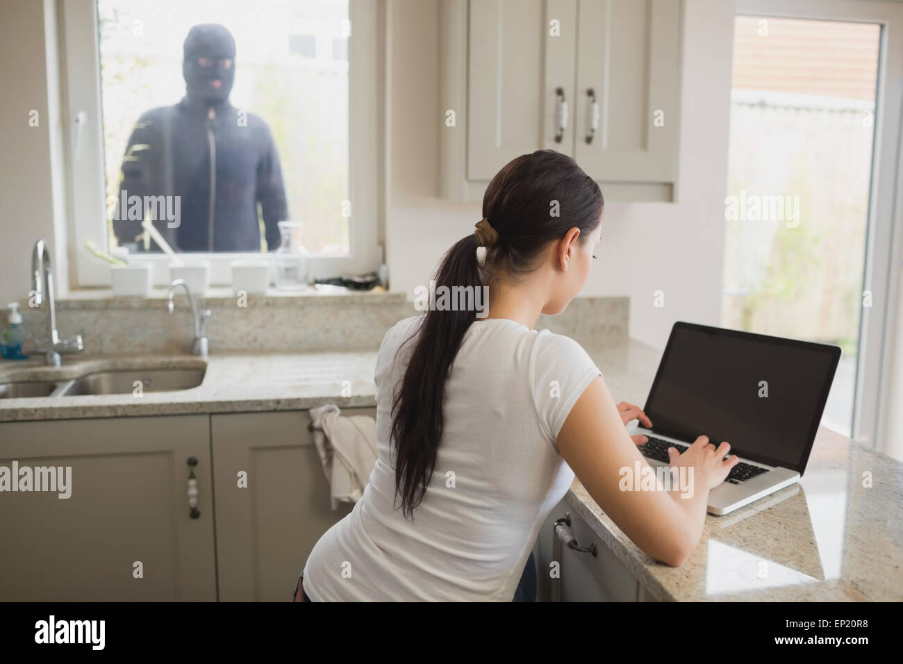 Robber looking at woman using laptop through window Stock Photo - Alamy