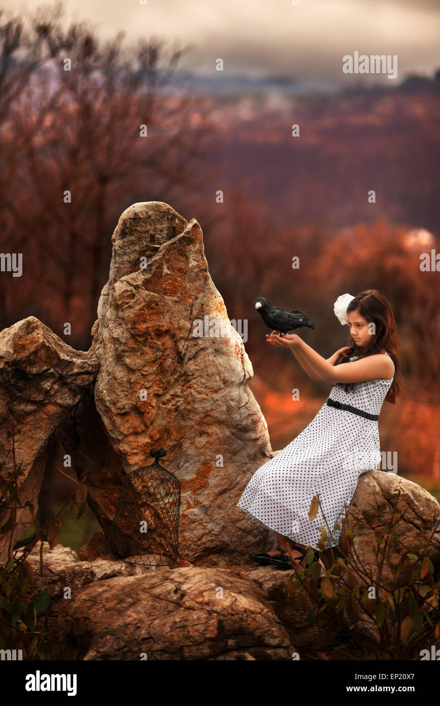 Girl sitting on rocks holding a stuffed black bird Stock Photo - Alamy