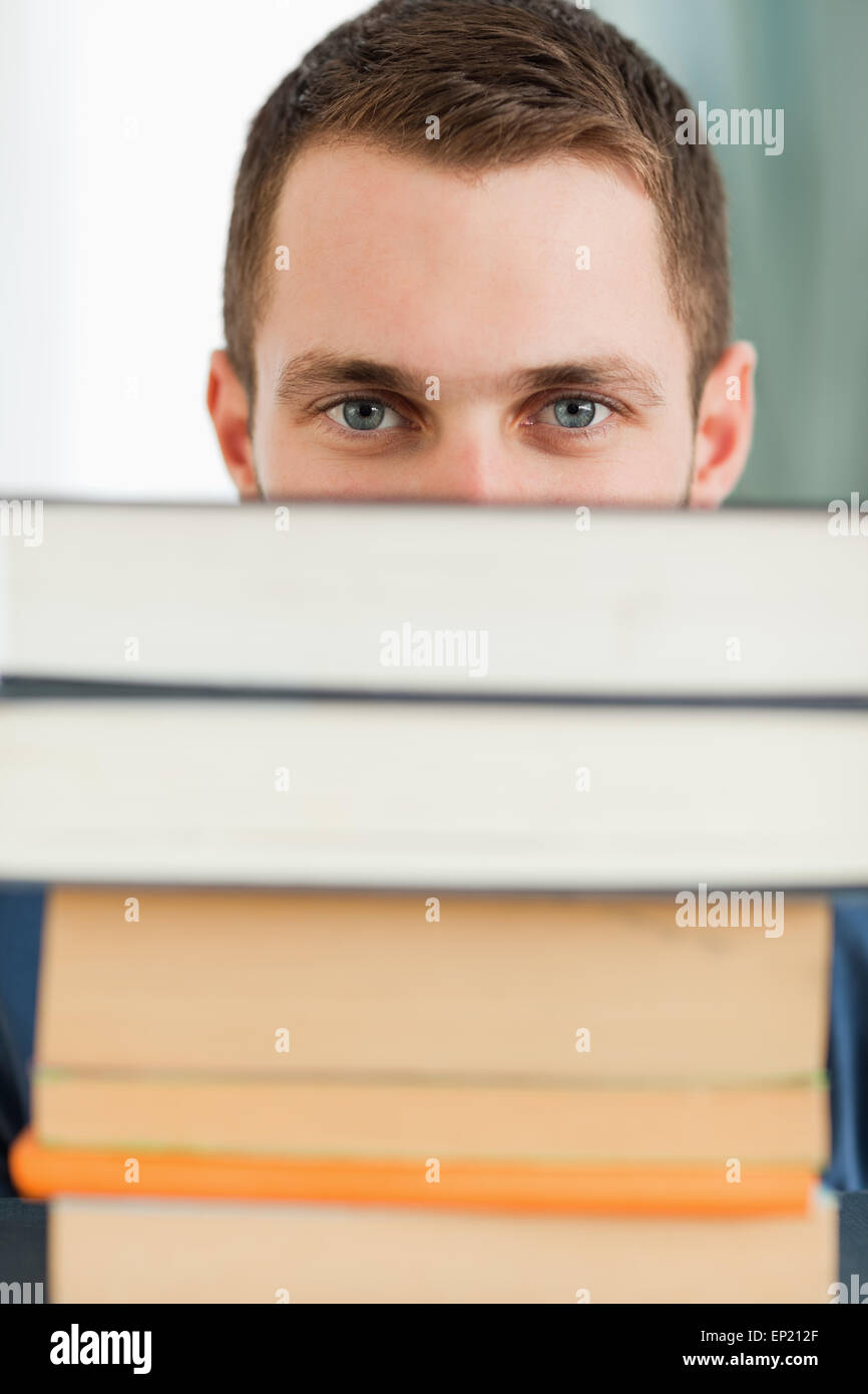 Close up of student hiding behind a stack of books Stock Photo - Alamy