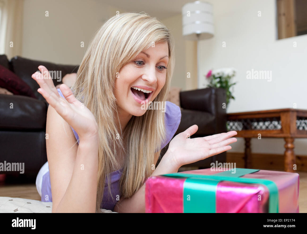 Surprised young woman opening gifts lying on the floor Stock Photo - Alamy