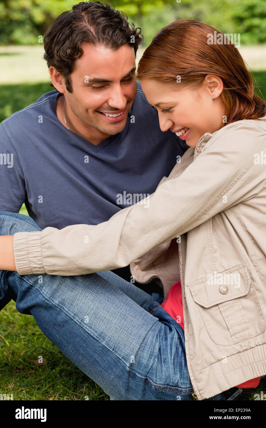 Two friends look happily towards the ground as they sit next to each ...
