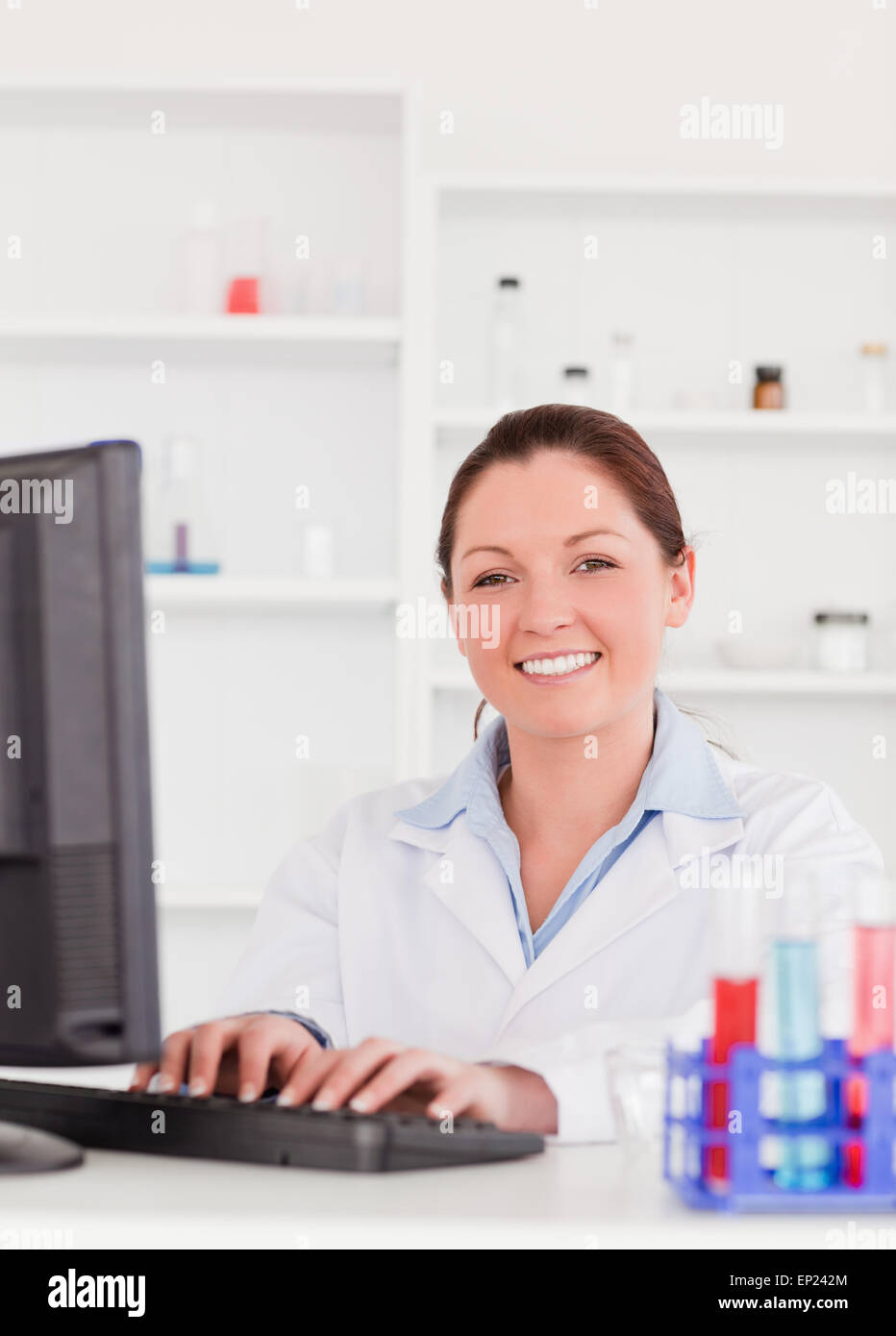 Smiling scientist typing a report with her computer looking at the ...