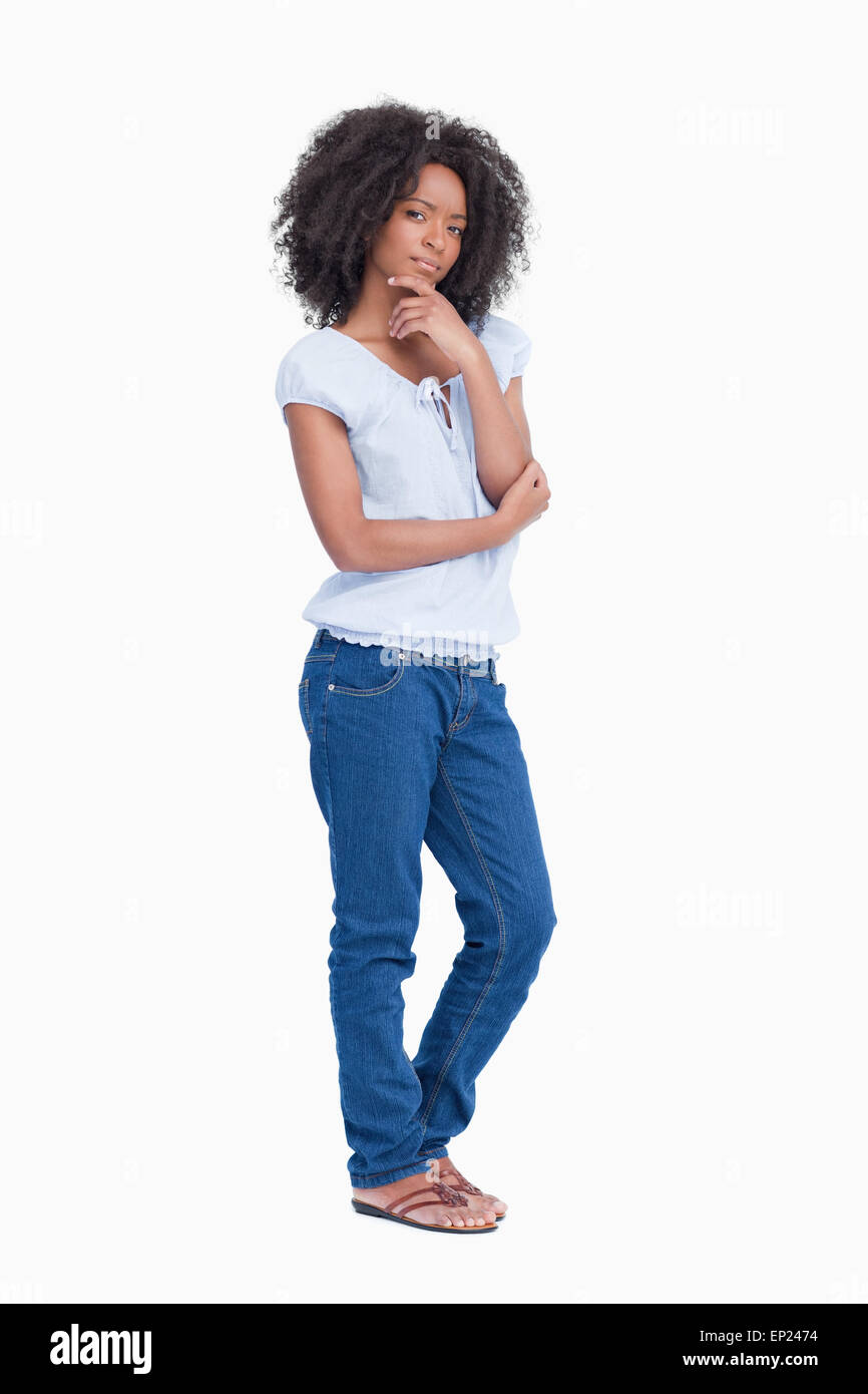 Young woman standing up while putting her fingers on her chin and ...