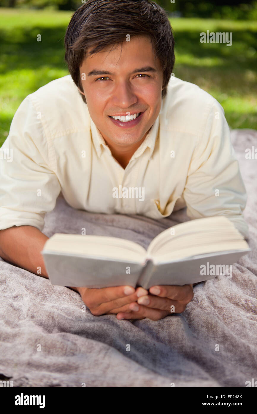 Man smiling while reading a book as he lies on a blanket Stock Photo ...