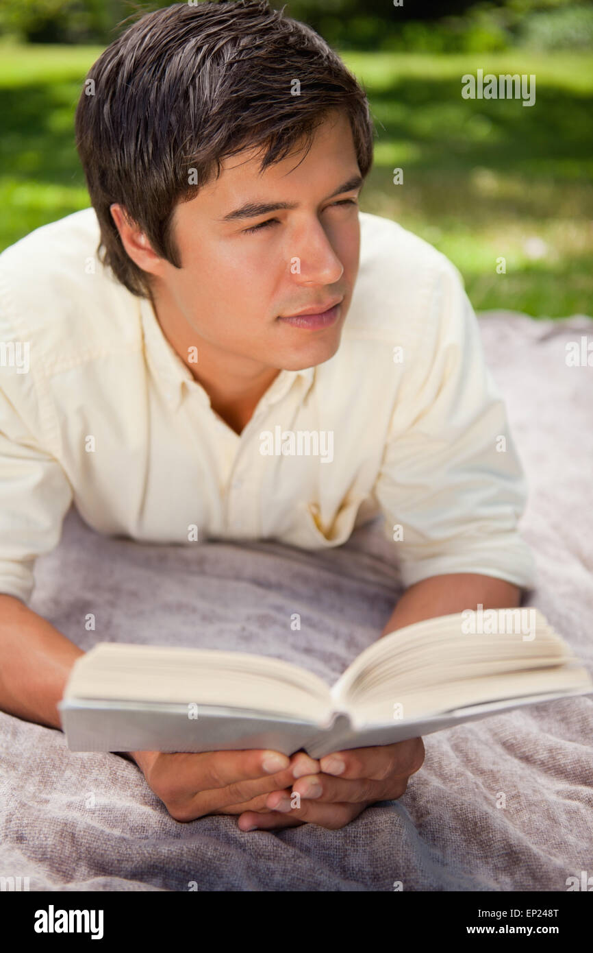 Man looking to his side while reading a book as he lies on a blanket ...