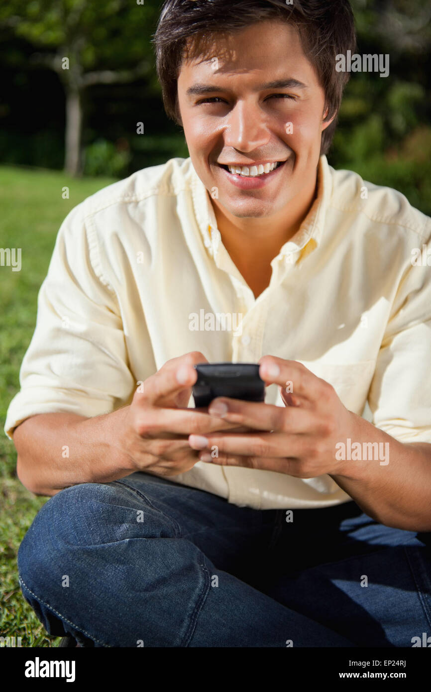 Man smiling while writing a text message as he is sitting down Stock ...