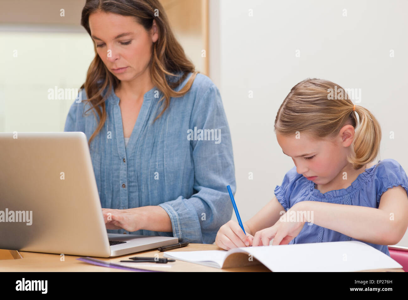 Girl doing her homework while her mother is using laptop Stock Photo ...