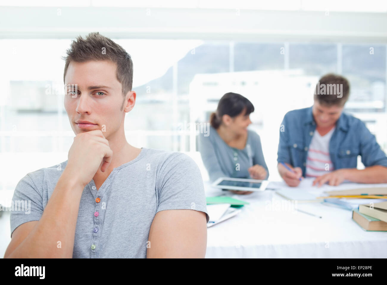 A thinking student looking into the camera with his friends behind him ...