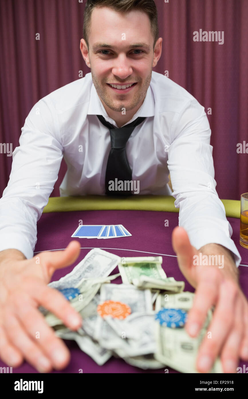 Happy man at poker table taking his winnings Stock Photo - Alamy