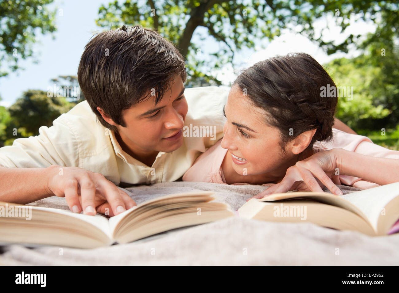 Two friends looking at each other while reading books on a blanket ...