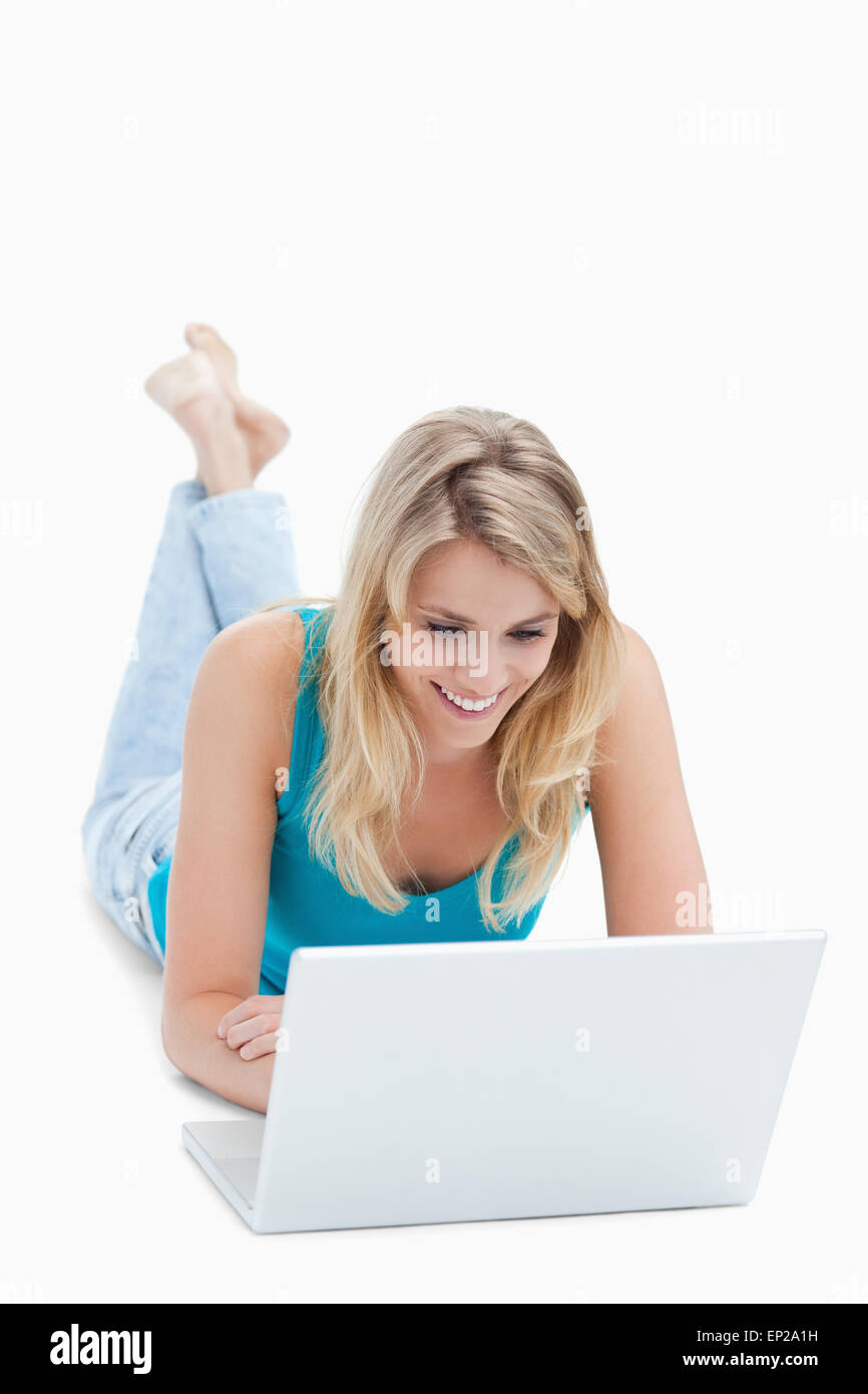 A smiling woman with a laptop is lying on the ground with her legs up ...
